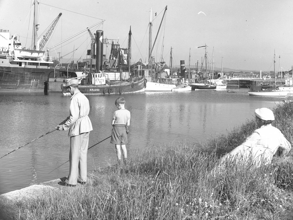 A man and boy fishing in Glasson Dock, lady looking on, various boats ...