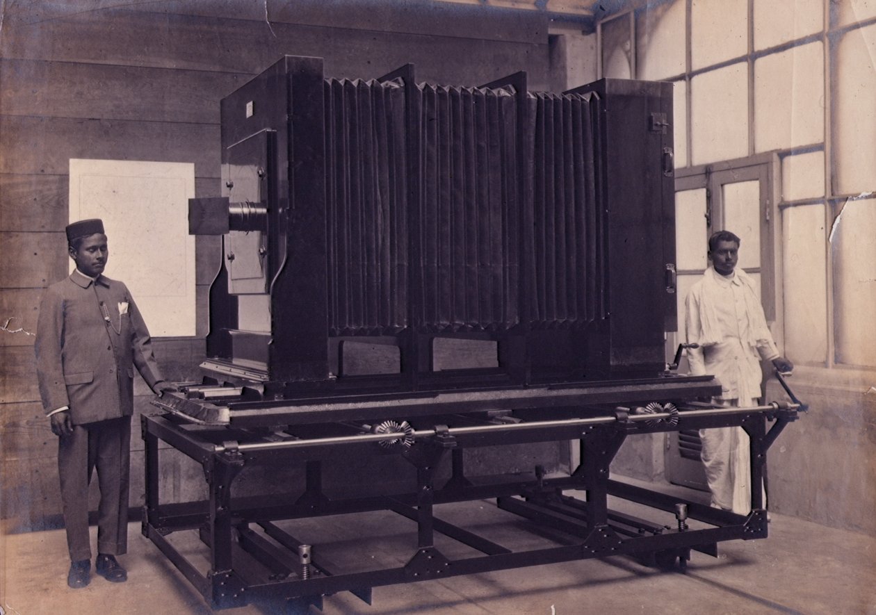 Two Indian assistants standing beside the massive camera in the ...