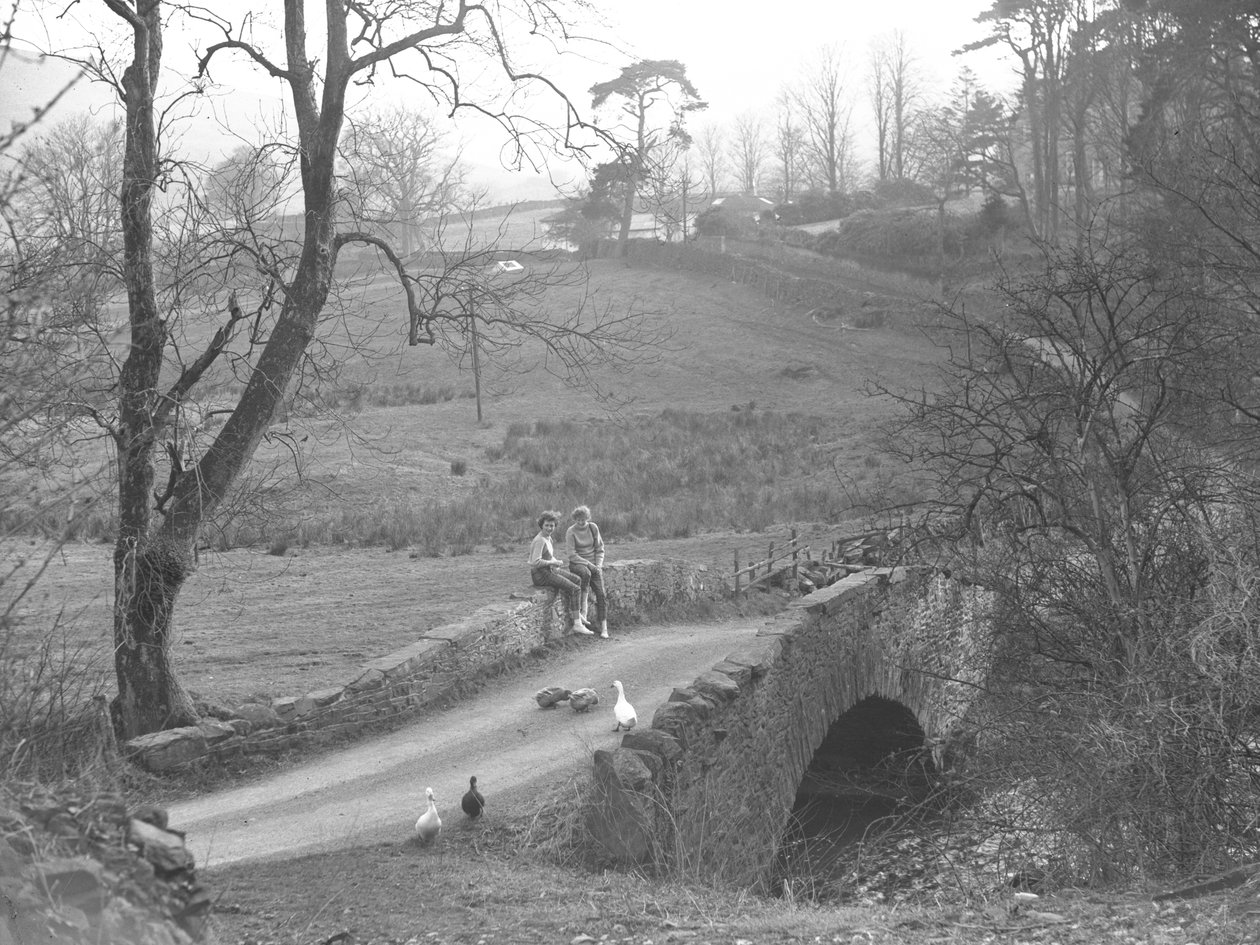 Two girls sitting on a stone bridge over the river Cocker at the bottom ...